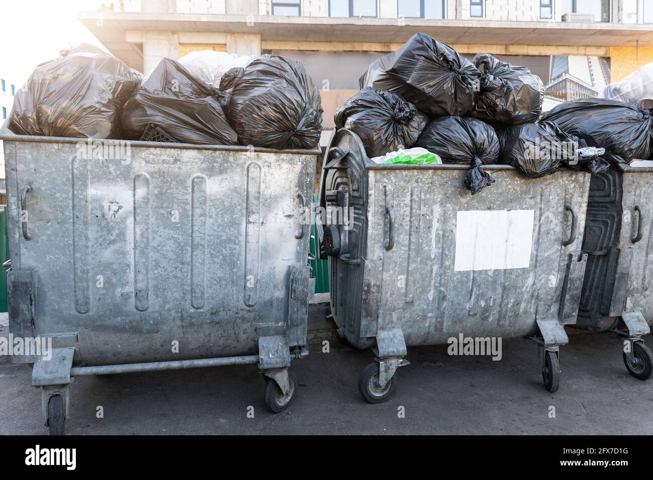 Rows of many big metal overloaded dumpster cans full of black plastic ...