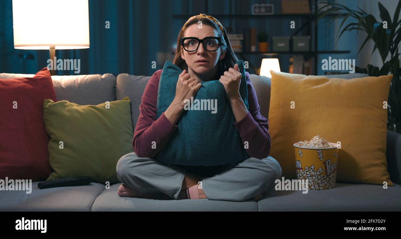 Frightened woman sitting on the couch and watching a horror movie on TV ...