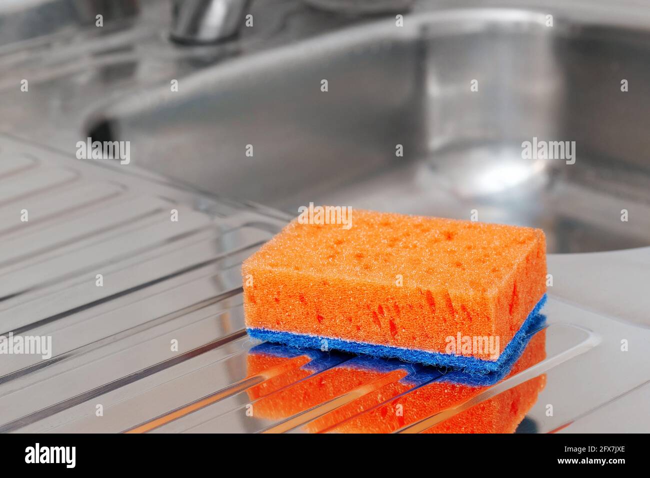 Closeup of orange sponge and strainer stopper in stainless steel sink ...
