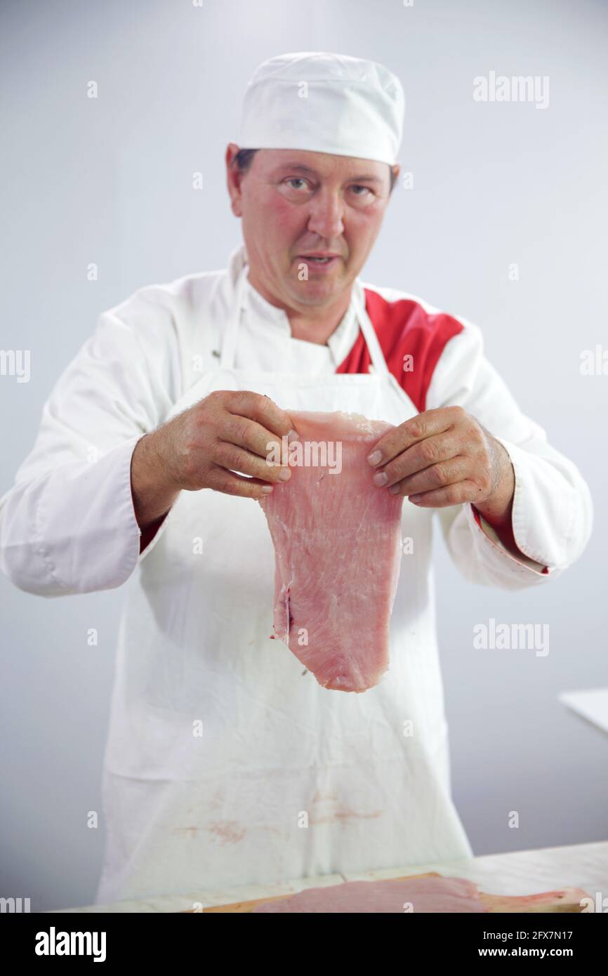 A vertical shot of a butcher holding a piece of freshly cut turkey meat ...
