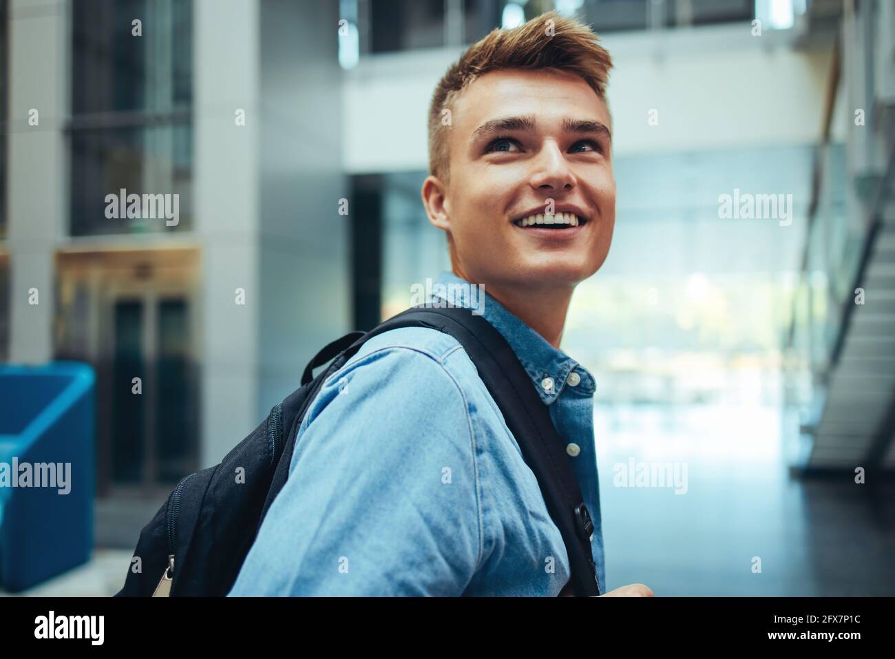 Happy young male student looking back and smiling in college ...