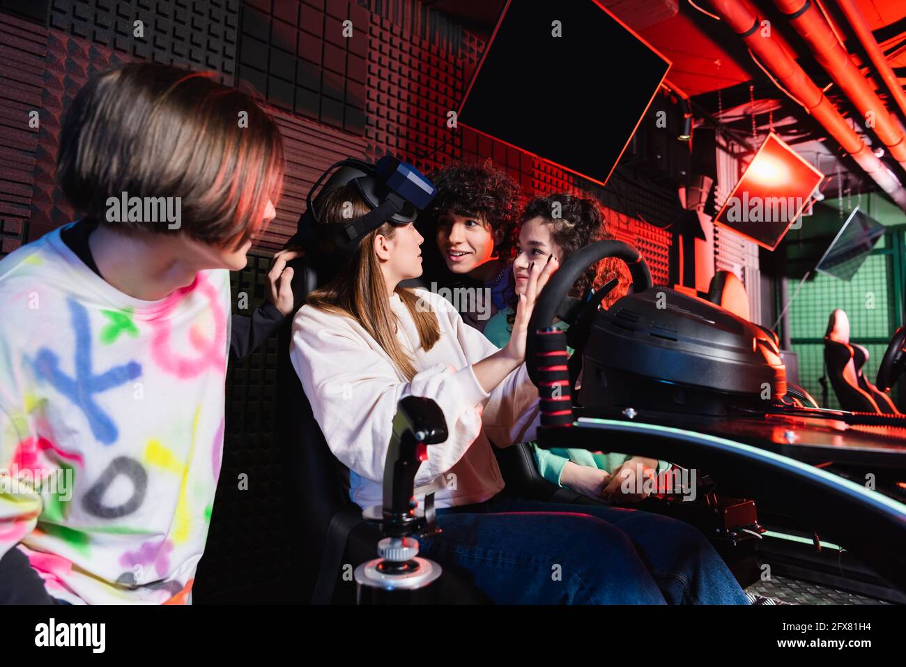 excited multiethnic friends looking at girl on car racing simulator ...