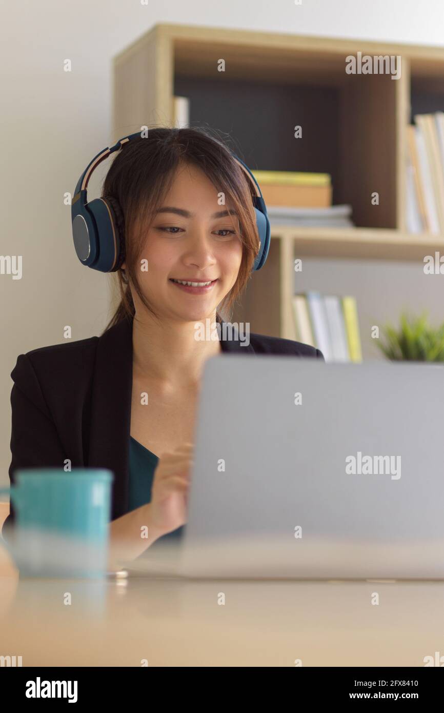 Portrait of happy businesswoman smiling and using headphone while working with laptop in home ...