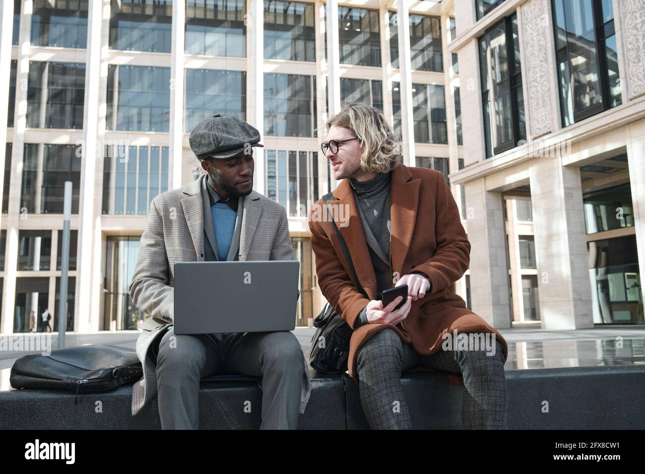 Two young men using laptop and working together while sitting in the ...