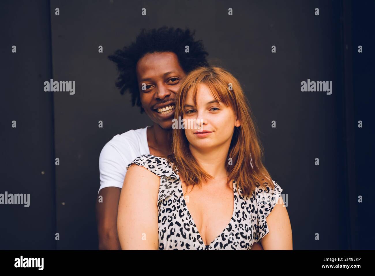 Multi-ethnic couple hugging front of a grey background Stock Photo - Alamy