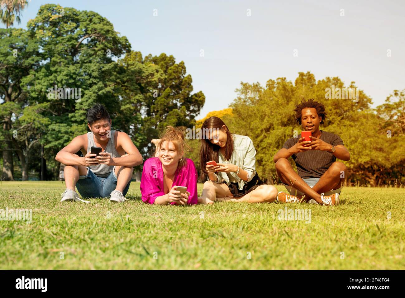 A multi-ethnic group of friends using their mobile phones while laying ...