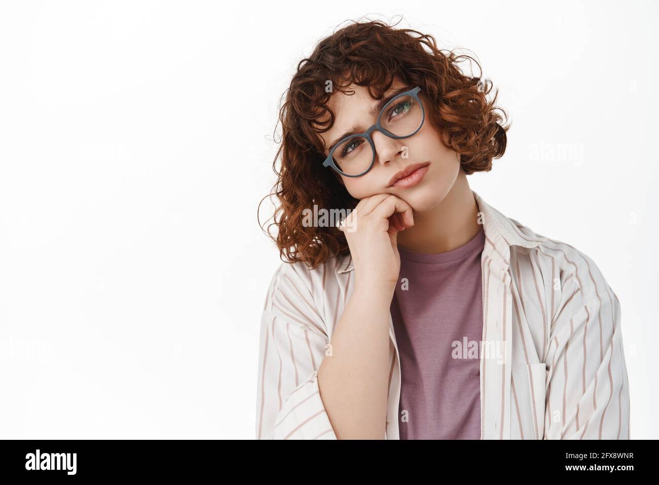 Portrait of bored curly girl student in glasses, leaning on hand and ...