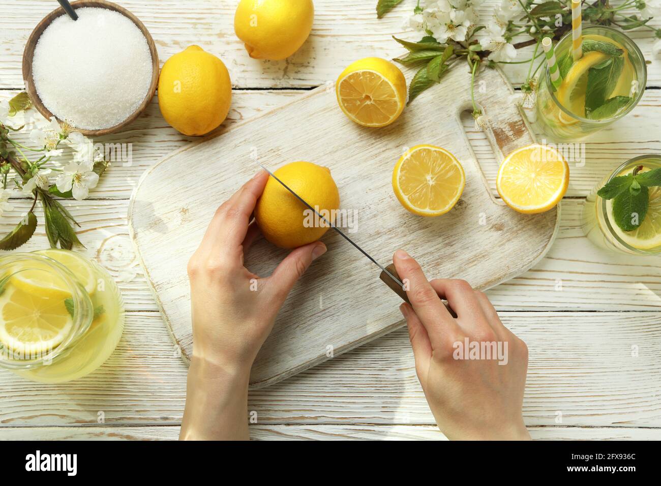 Female hands cuts lemon for making lemonade on white wooden background ...