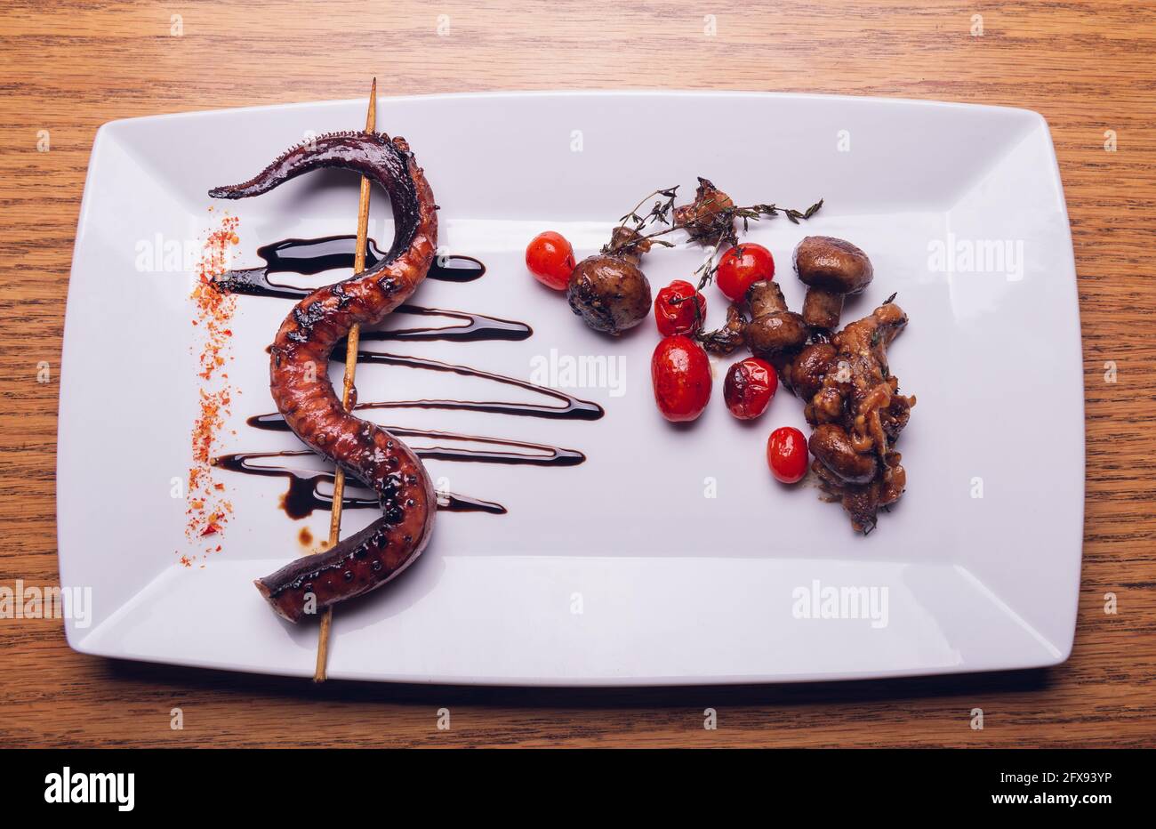Top view of an octopus tentacle on a stick served with tomatoes and ...