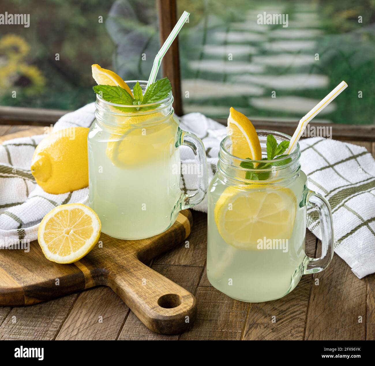 Two glasses of lemonade with lemon slices on a wooden table by a window ...