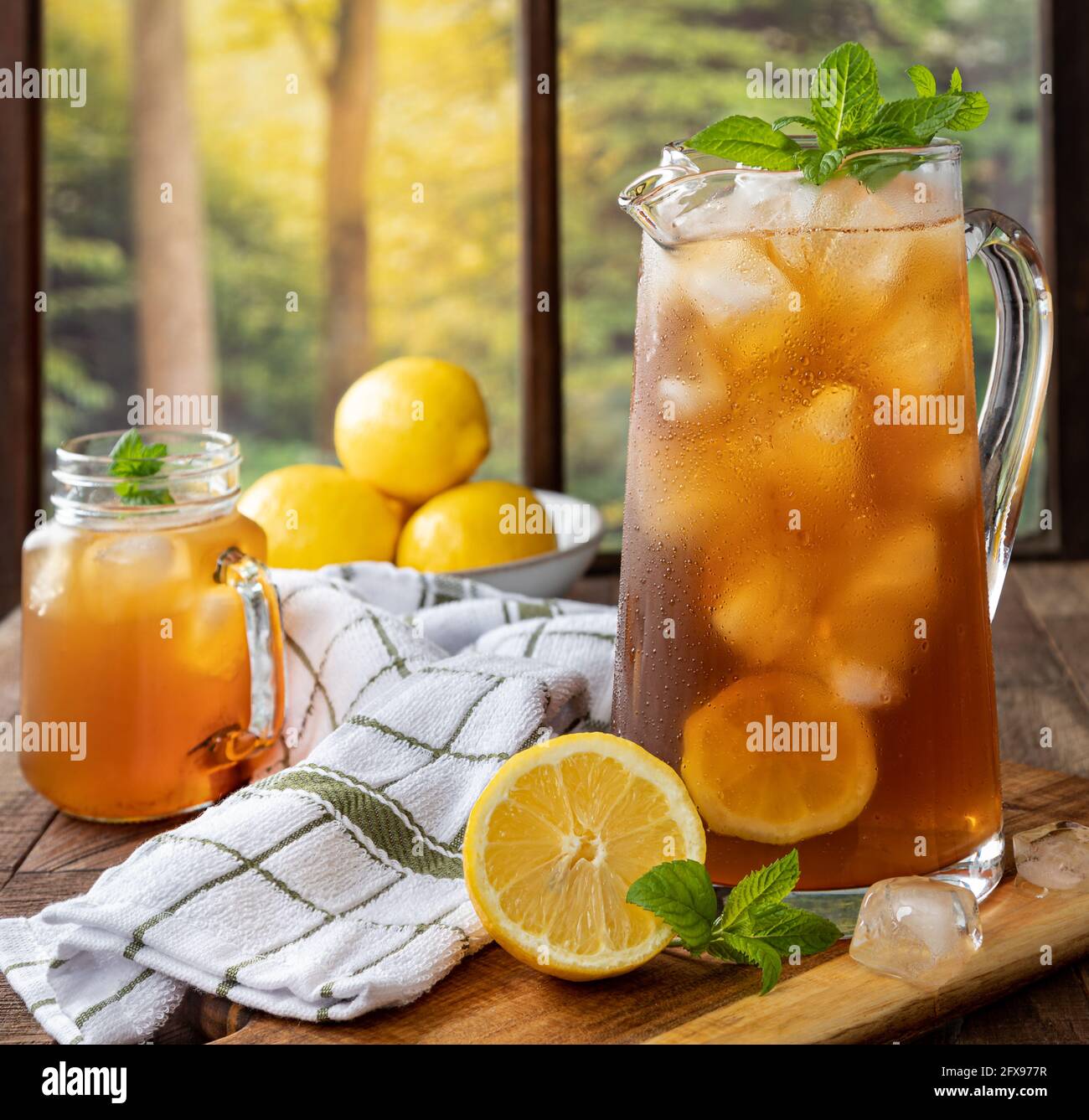 Pitcher of iced tea with lemon and mint on a wooden table with rural ...