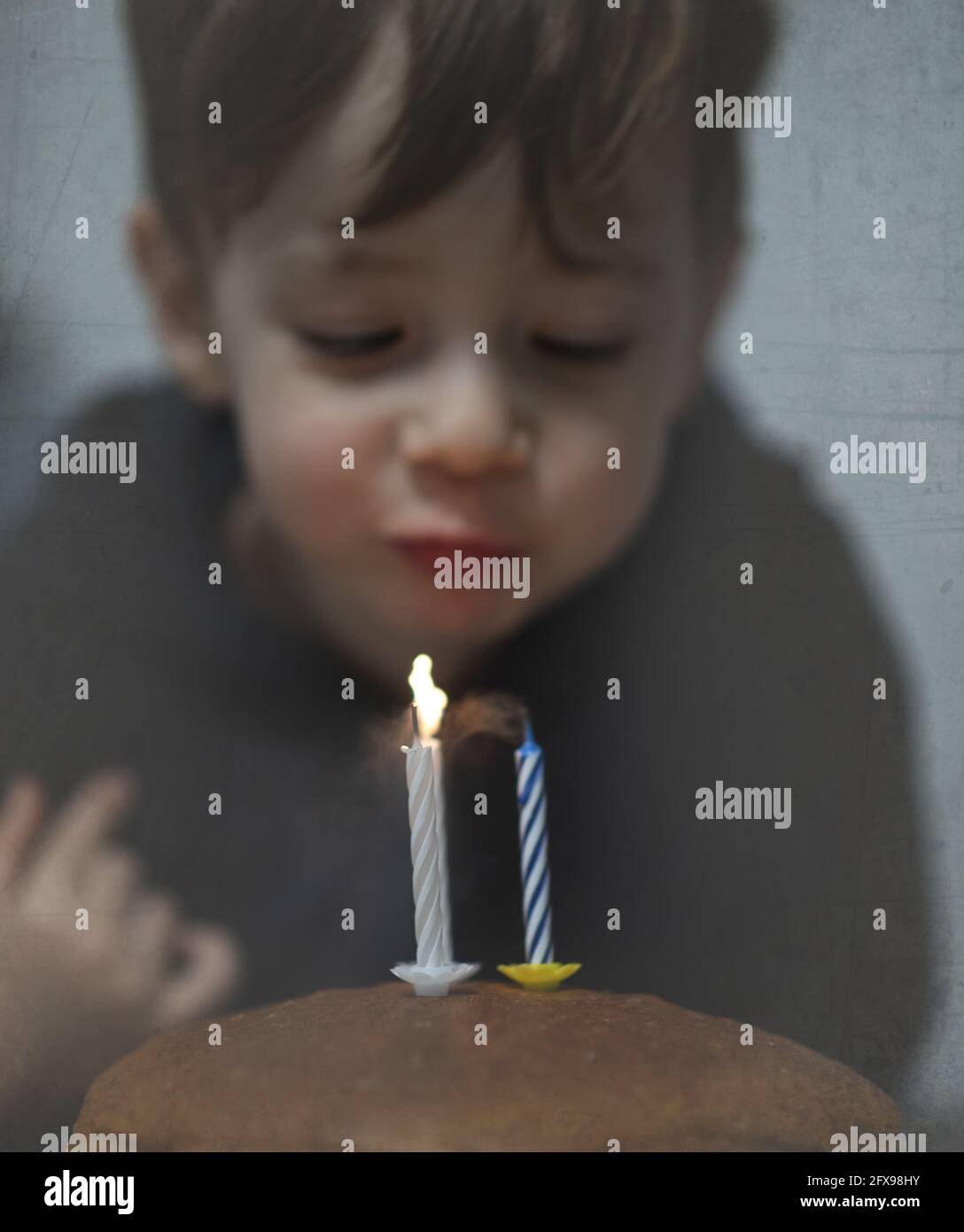 Vertical shot of a young Caucasian boy blowing two candles on a cake ...