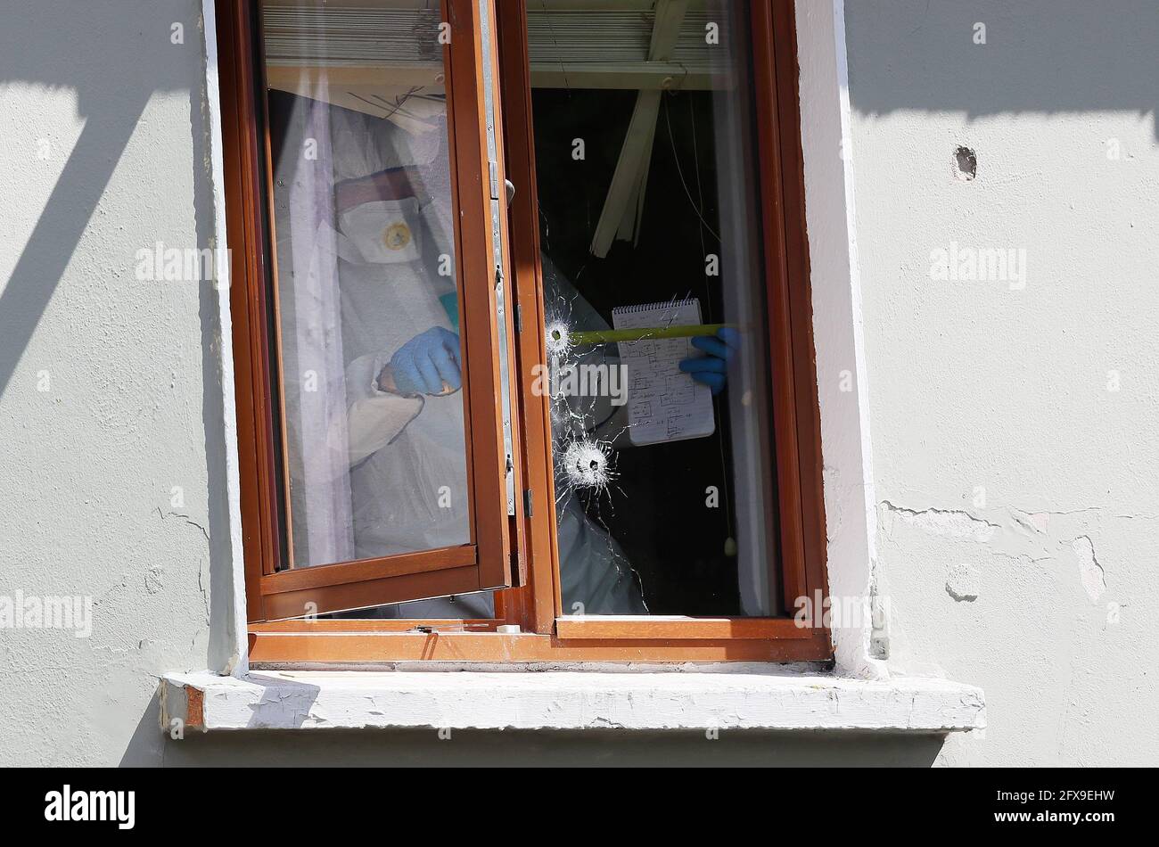 Forensic officers inspect bullet holes in a window at the scene in west ...