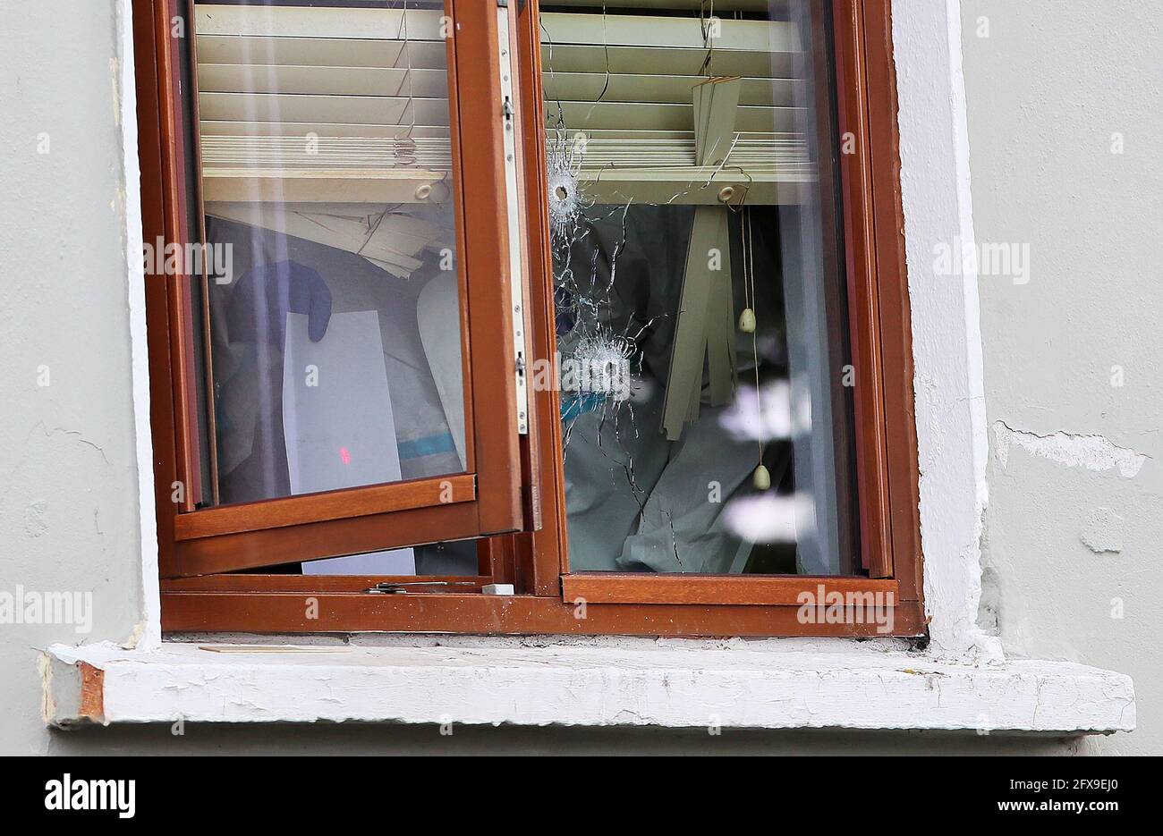Forensic officers inspect bullet holes in a window at the scene in west ...