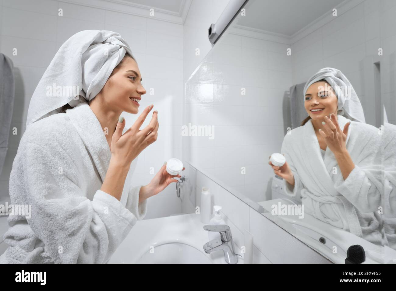 Side View Of Smiling Cute Young Woman Apply Facial Cream Look In Mirror