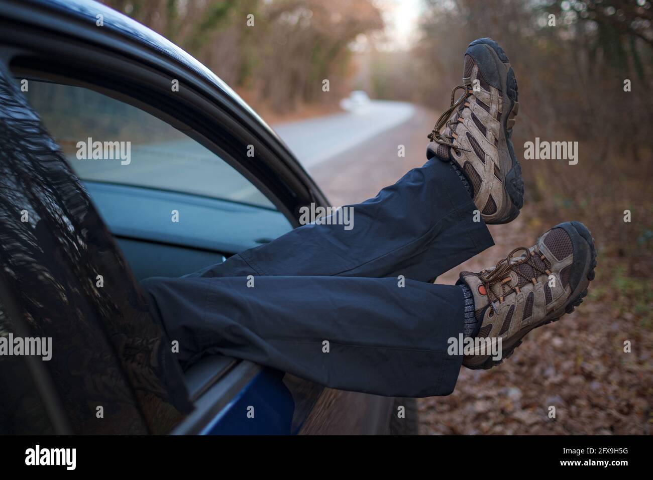 male feet in trekking boots sticking out the car window. Autumn car ...