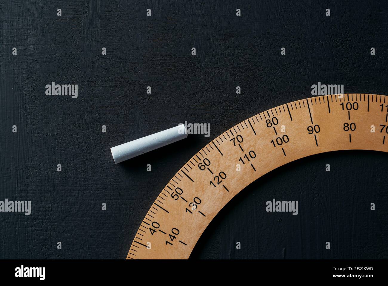 high angle view of a piece of chalk and a wooden protractor on a dark ...