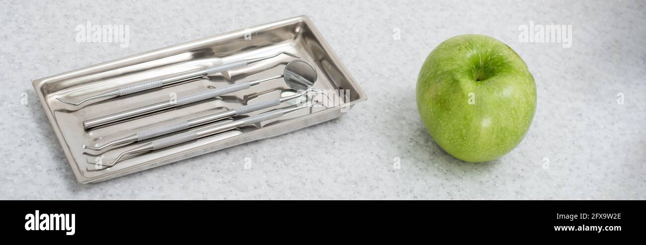 high angle view of metal dental tools in tray and green apple on ...