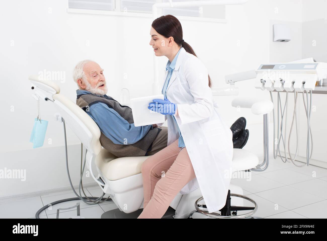 smiling dentist showing tablet to elderly patient in dental clinic ...
