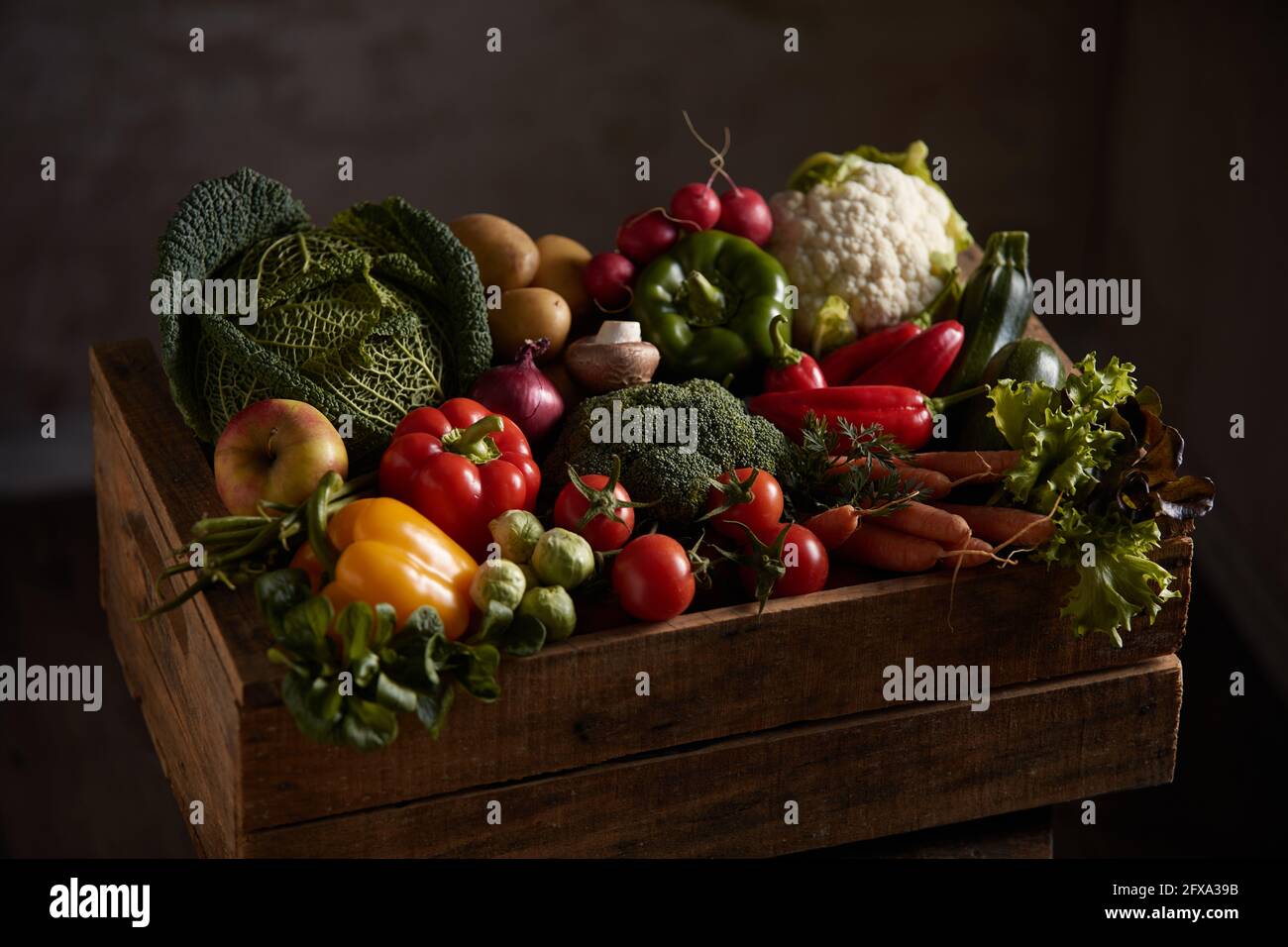 Wooden crate with assorted fresh vegetables placed against dark ...