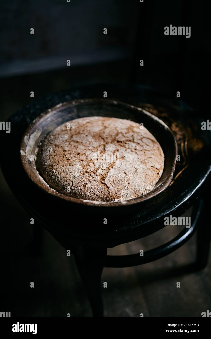 From above bowl with loaf of rye bread placed on chair in dim room ...