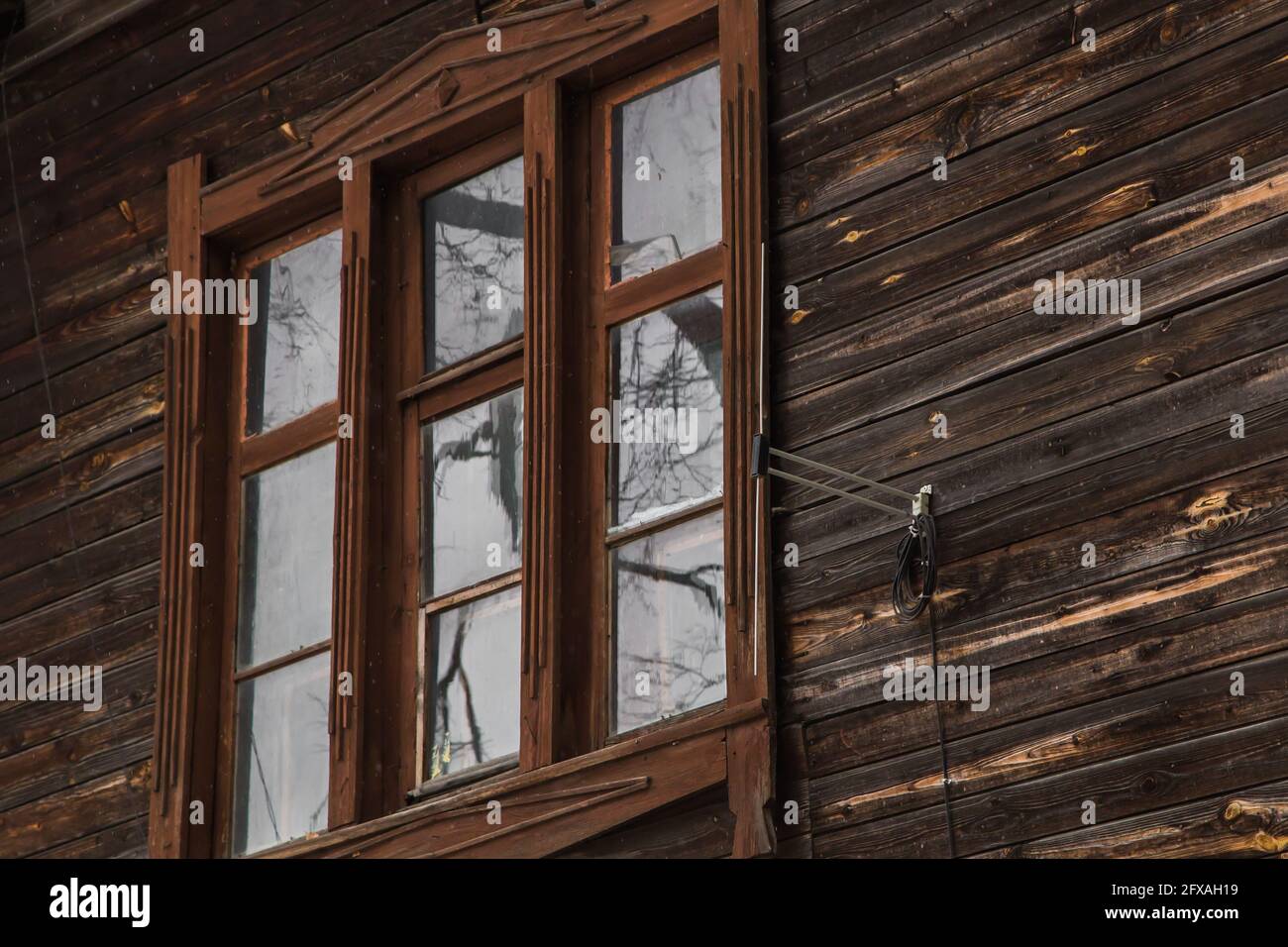 A wooden window in an old planked building with an antenna on the wall ...