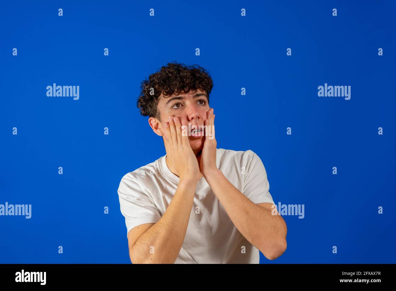Attractive young man with curly hair with hands on face with scared ...