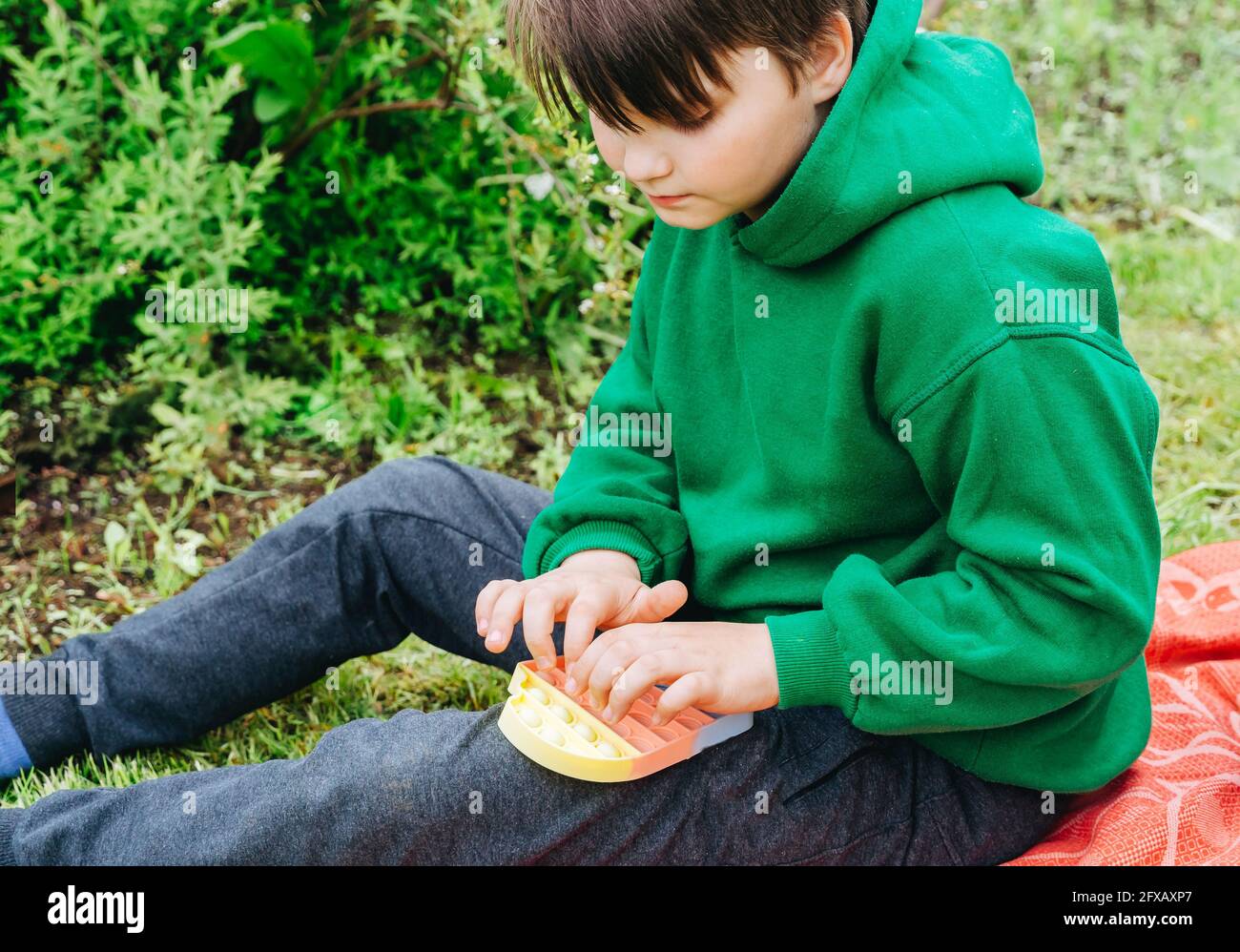 Boy with rainbow Pop It Fidget in hands. Teen in green Playing, Push ...
