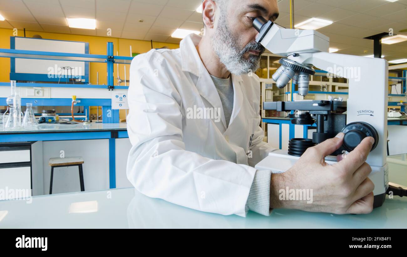 Mature scientist male in his 50s wearing a lab coat looking through a ...