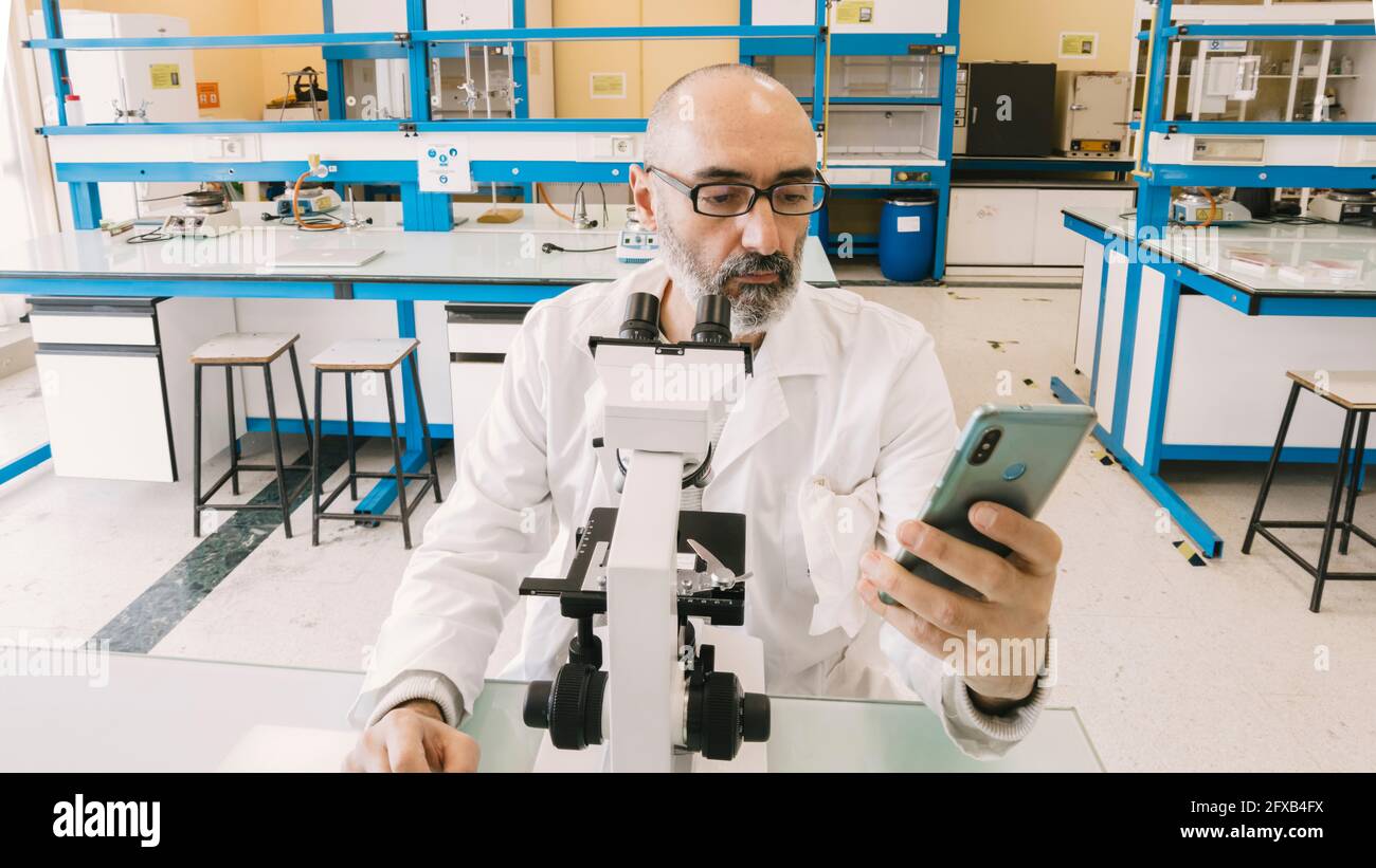 Mature scientist male in his 50s wearing a lab coat looking through a ...