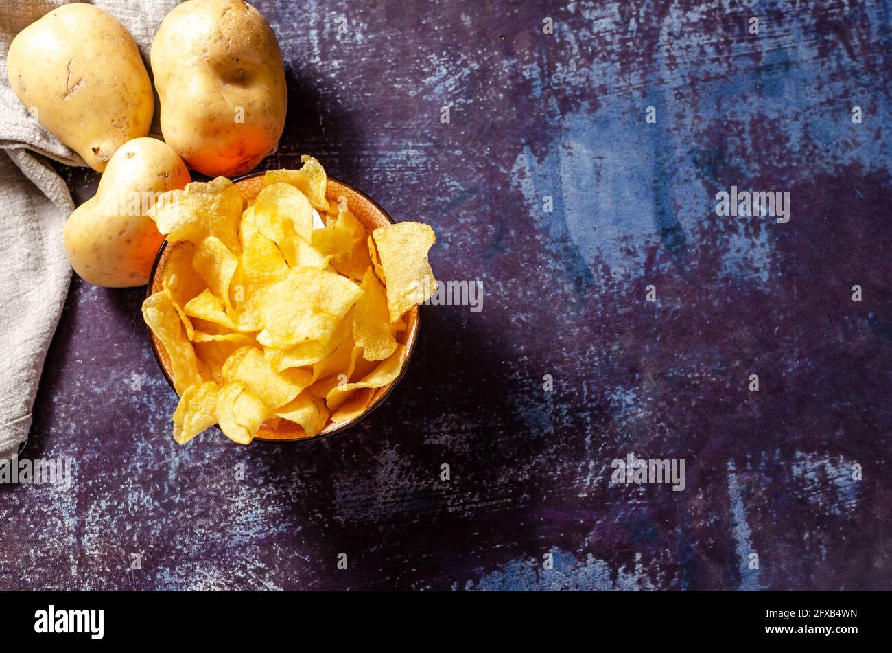 Still life of a bowl of potato chips with raw potatoes and a linen ...