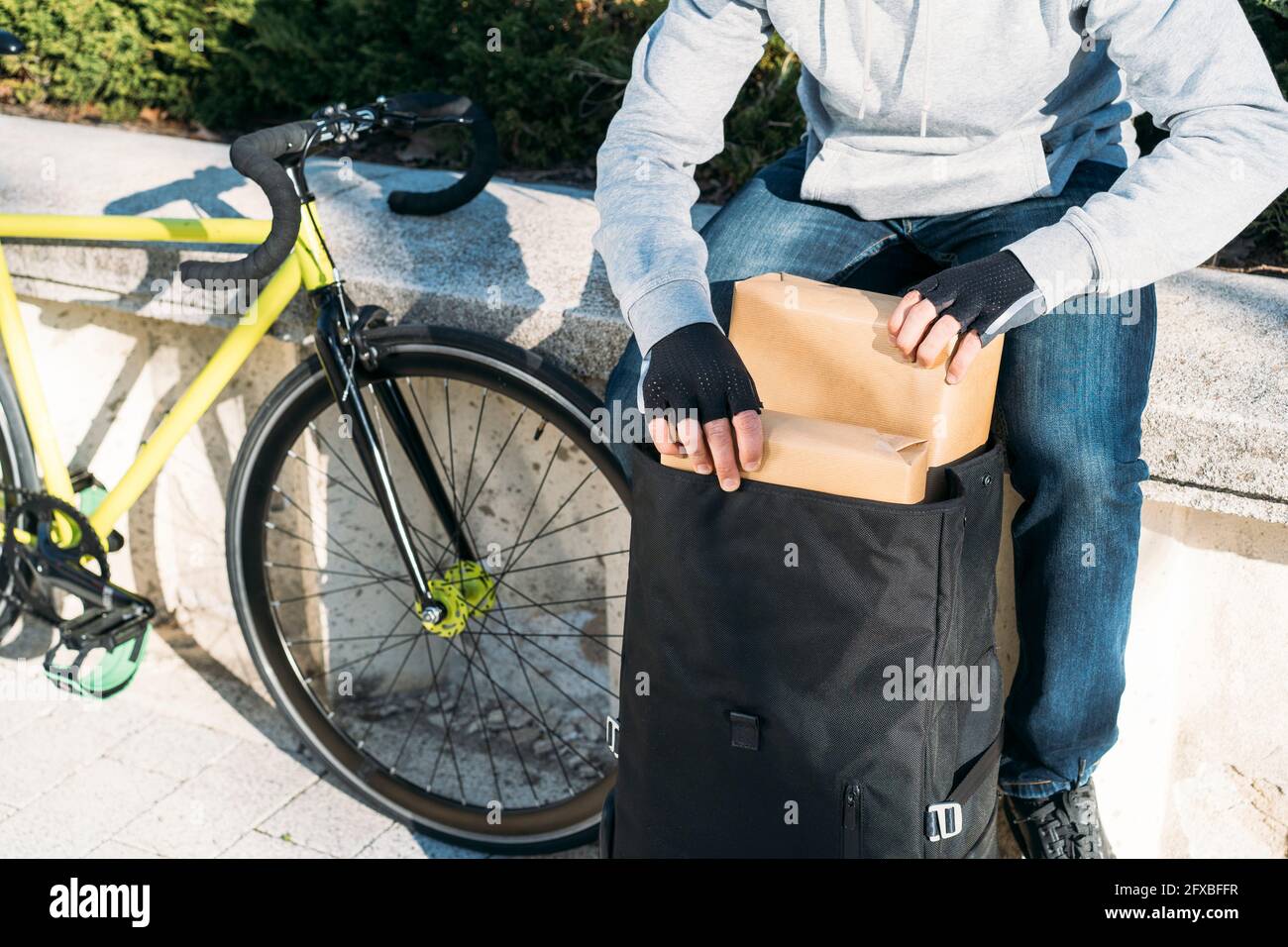 Delivery man removing package from backpack while sitting on retaining ...