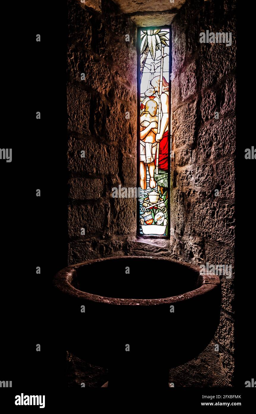 Baptismal font in a medieval church illuminated by a stained glass ...