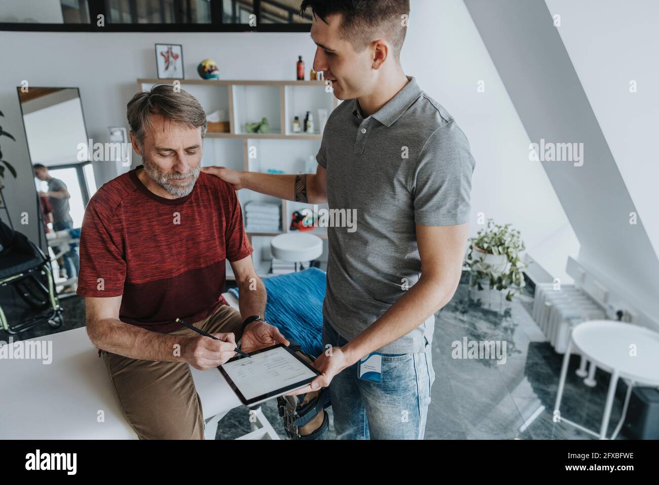 Male patient digitally signing form by physiotherapist in practice ...