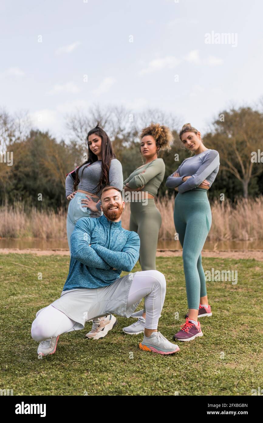 Female friends standing behind young man crouching in park Stock Photo ...