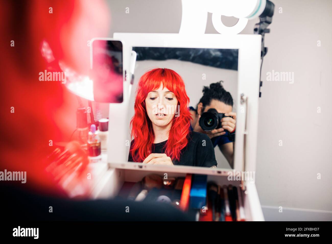 Man photographing female vlogger filming in front of mirror at studio ...