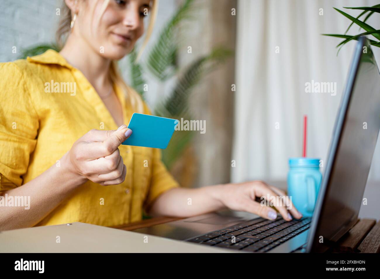 Female entrepreneur holding credit card while working on laptop at home ...
