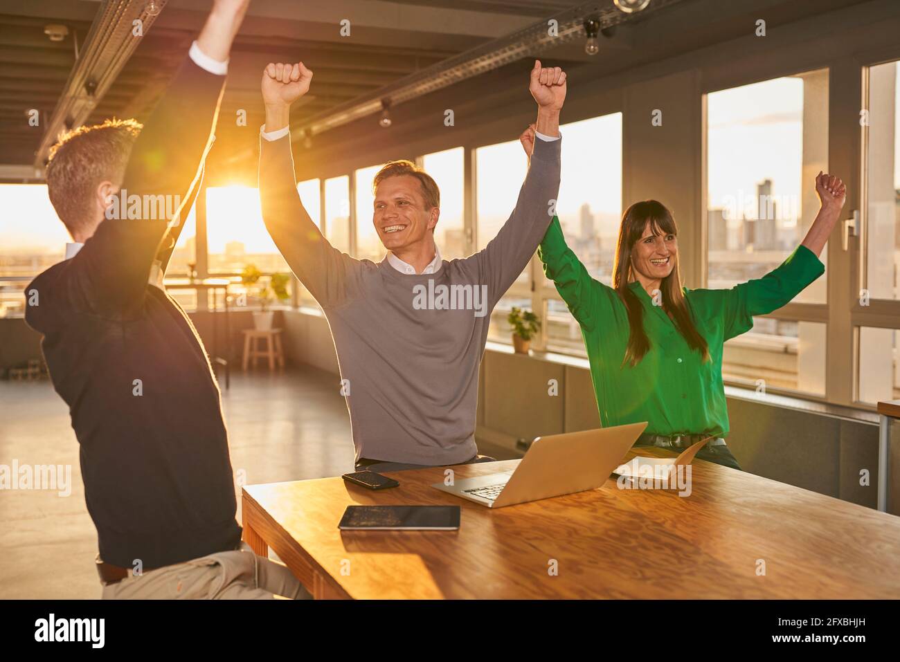 Cheerful male and female entrepreneurs cheering with arms raised in ...