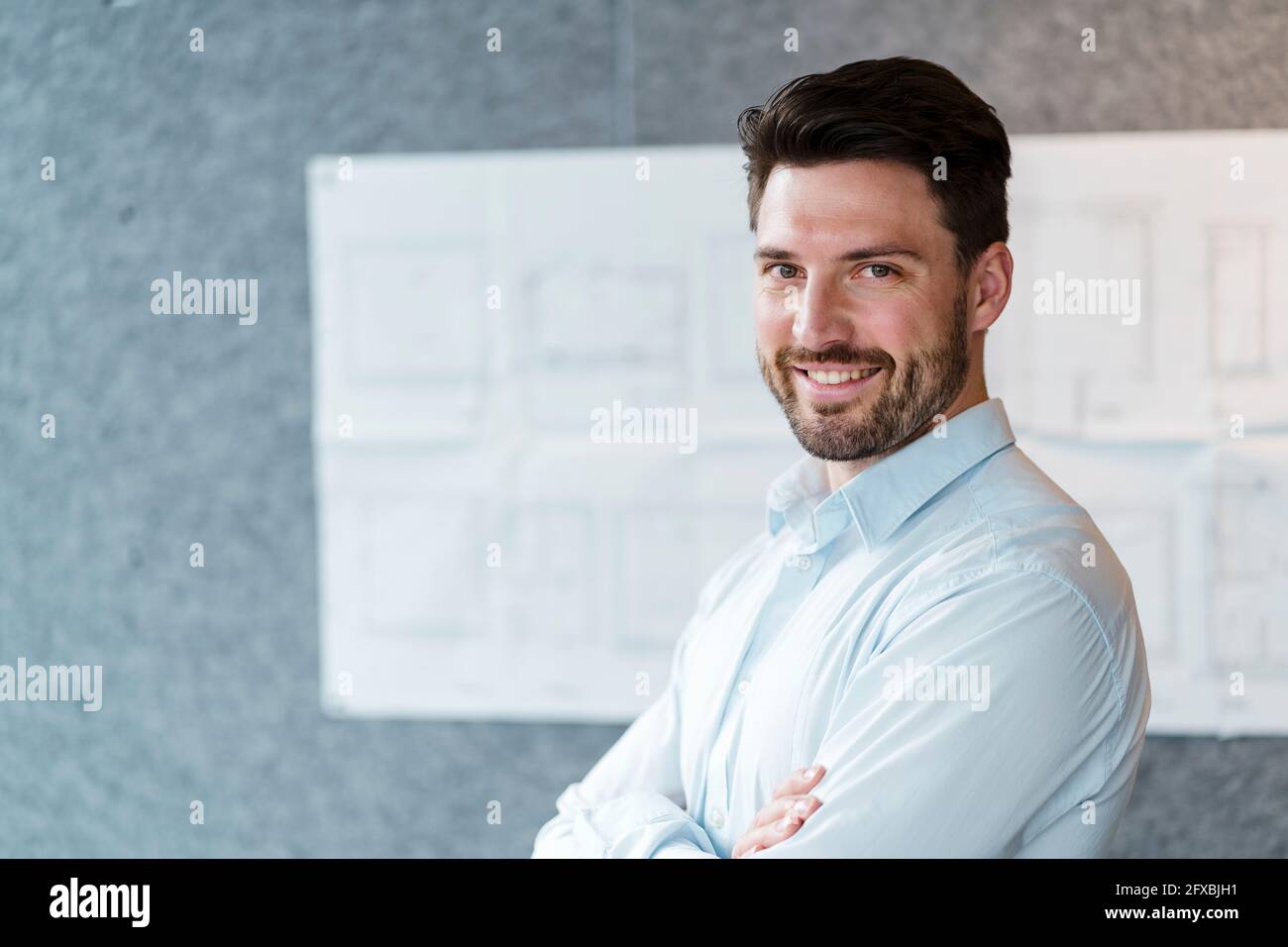 Smiling male professional with arms crossed at work place Stock Photo ...