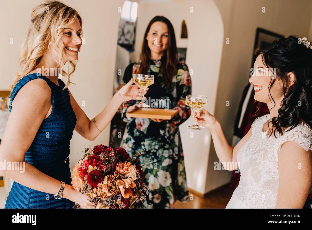 Happy bride with female friends drinking wine in domestic room Stock ...
