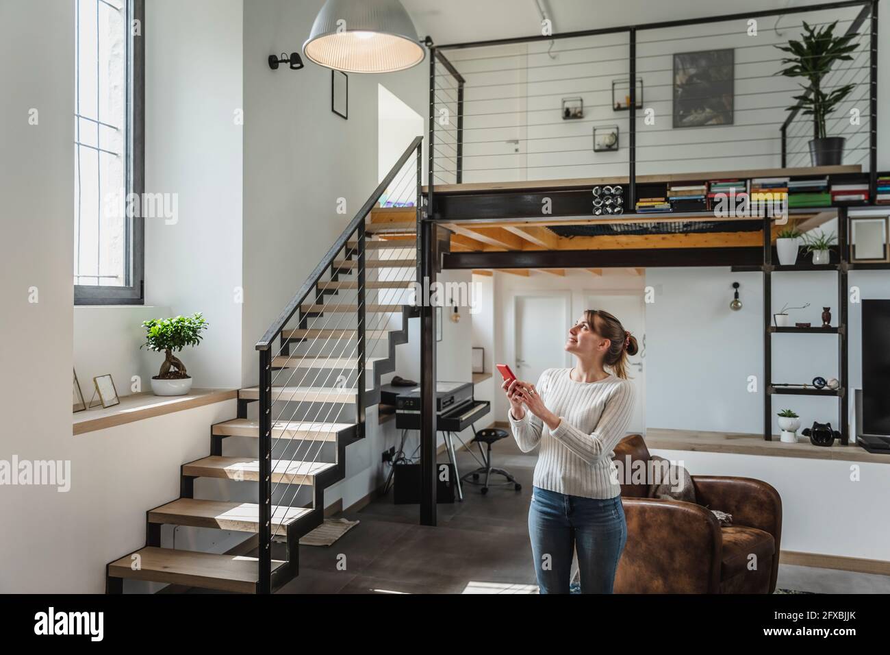 Young woman controlling smart home functions through mobile phone at ...