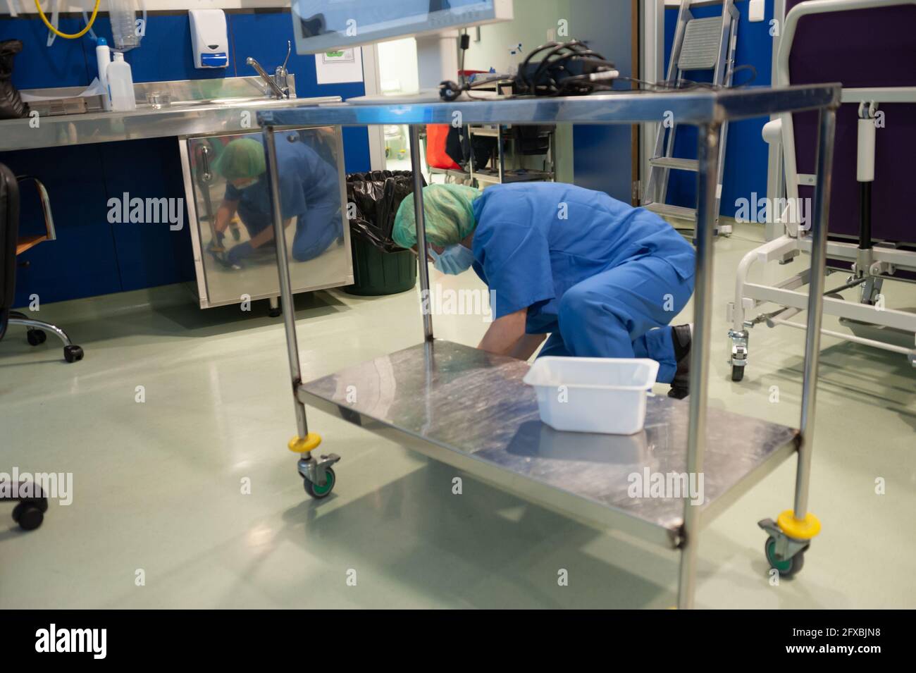 Woman from the cleaning service of a hospital crouching cleaning a ...
