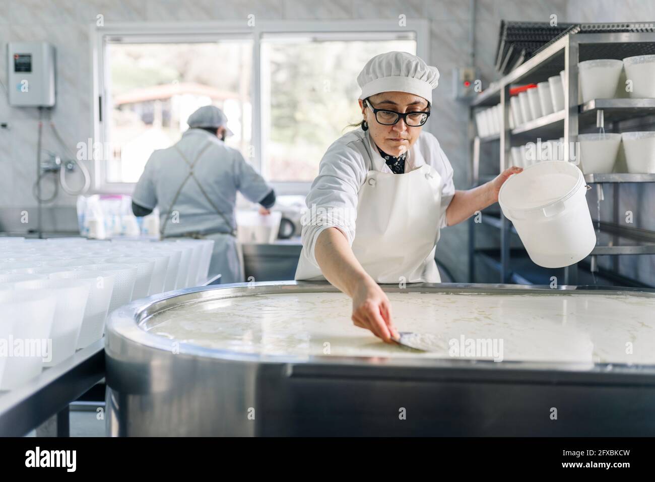 Female chef making cheese with colleague in background at factory Stock ...