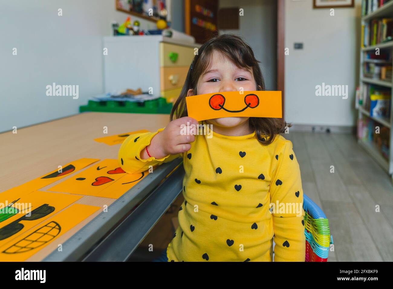 Cute girl holding smiling emoticon while playing at home Stock Photo ...