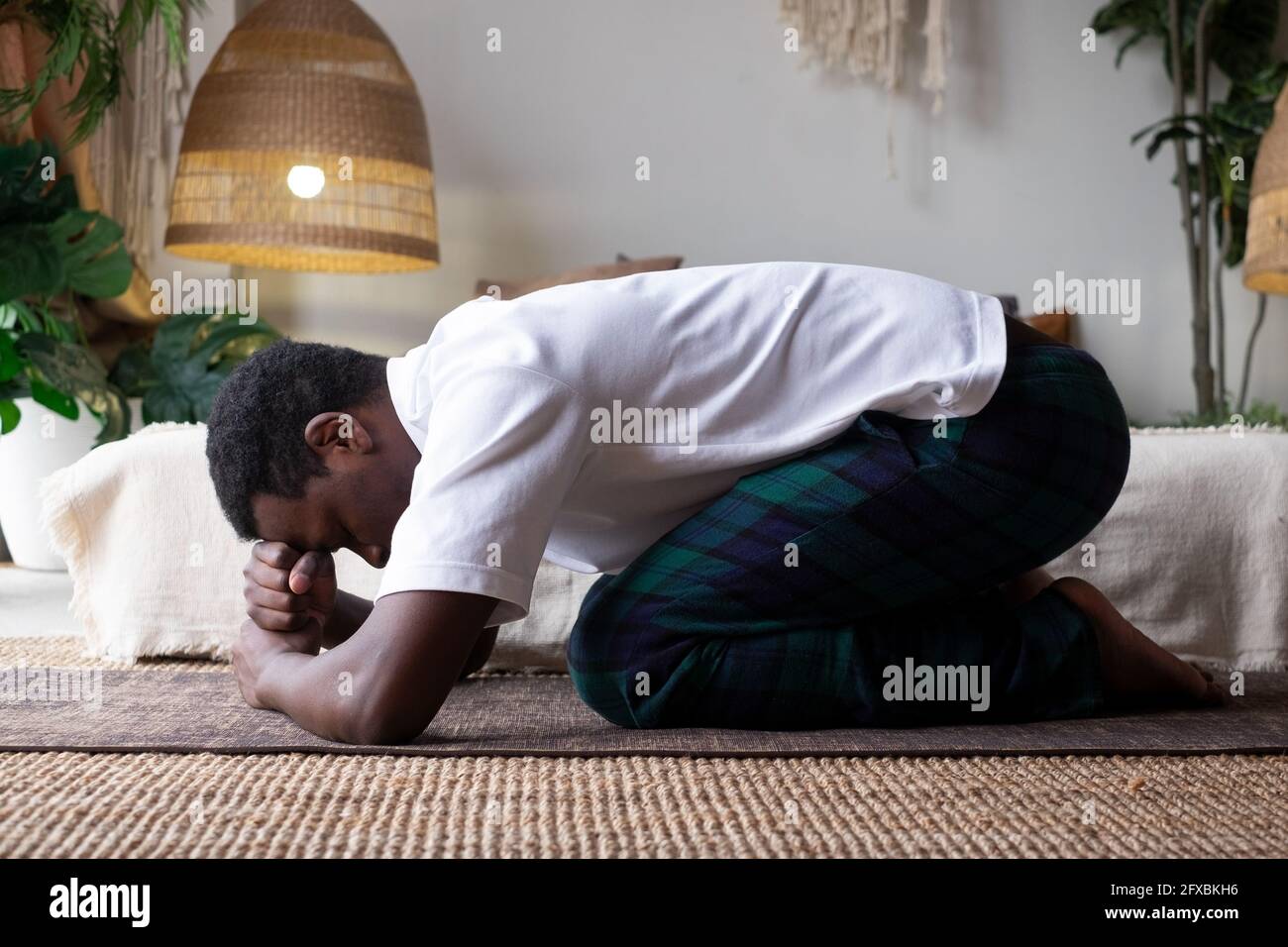 African man doing yoga at home, having rest in balasana or child pose ...