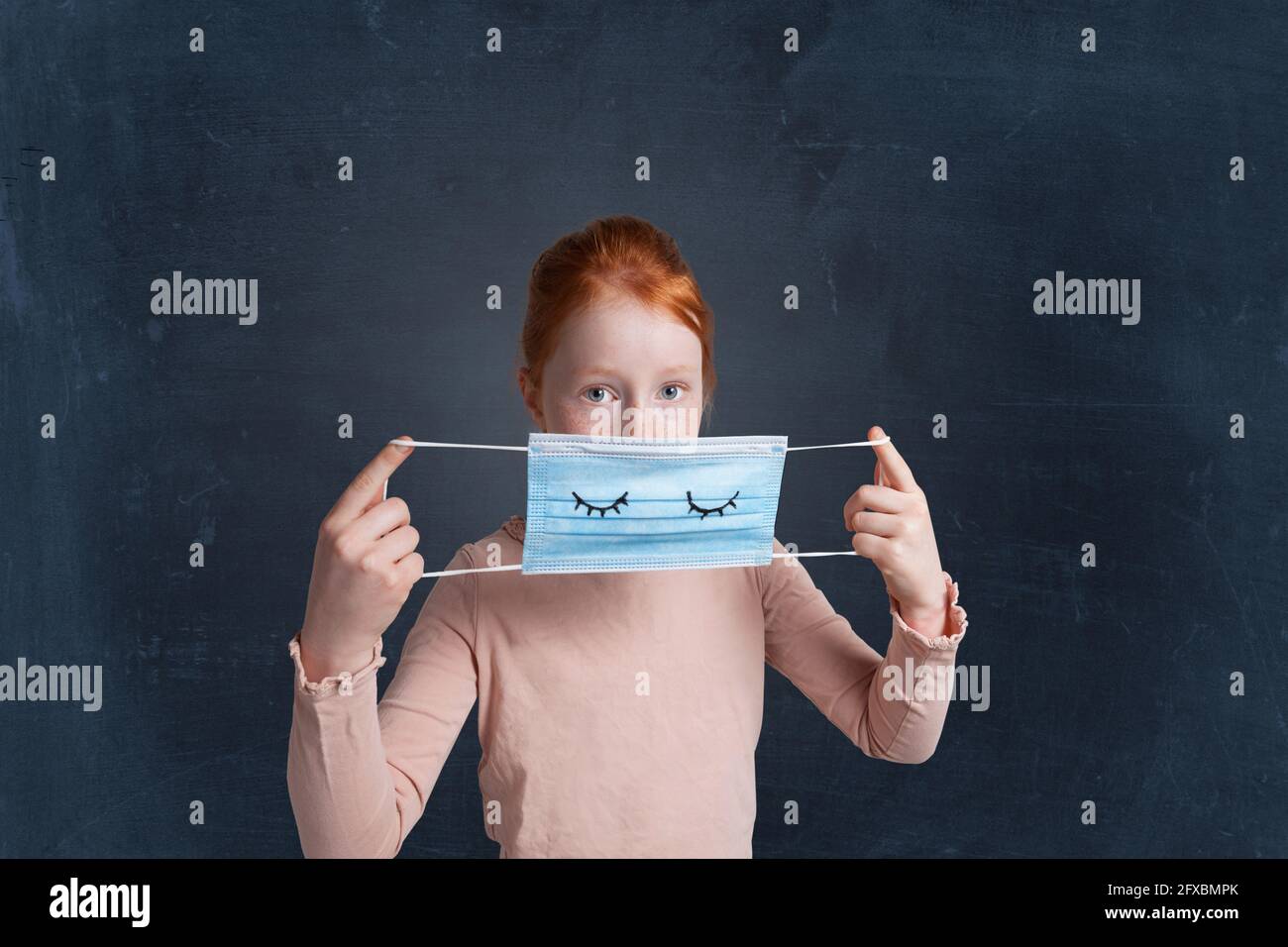 Girl pulling string of face mask against black background Stock Photo ...