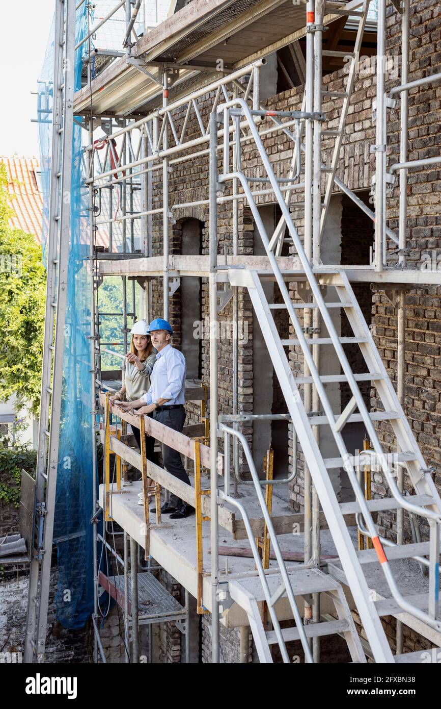 Female client showing construction to male architect while standing in ...