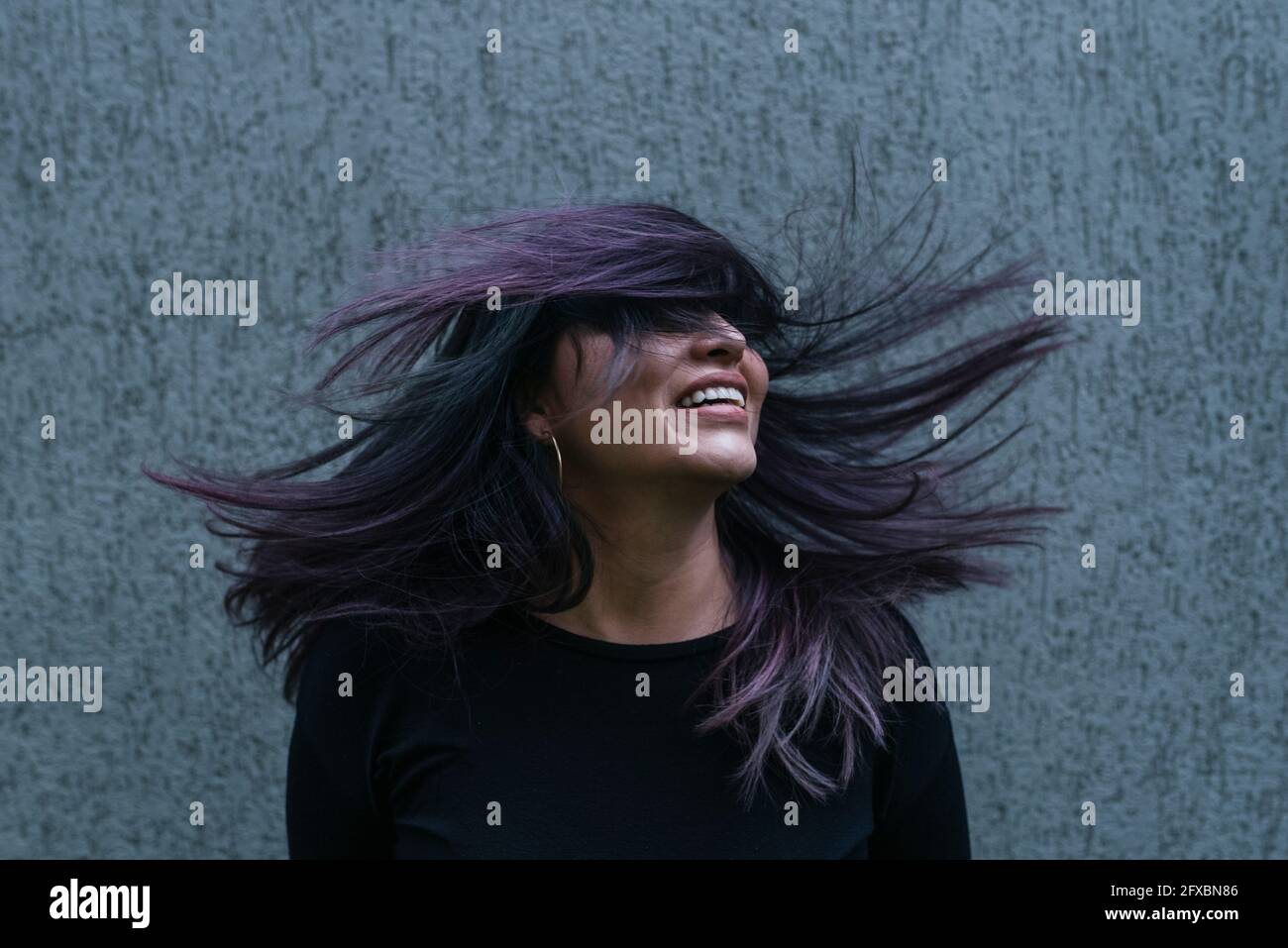 Playful woman tossing hair in front of wall Stock Photo - Alamy