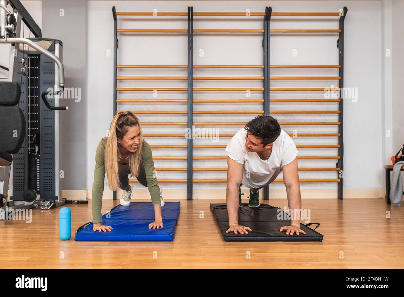 Smiling male and female athletes doing push-ups on exercise mat in gym ...