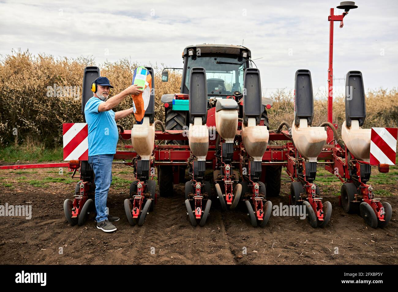 Male farmer wearing ear protectors while pouring corn in containers of ...